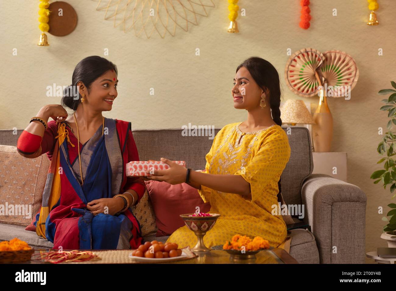 Bengali family exchanging gift while sitting together on sofa in living ...