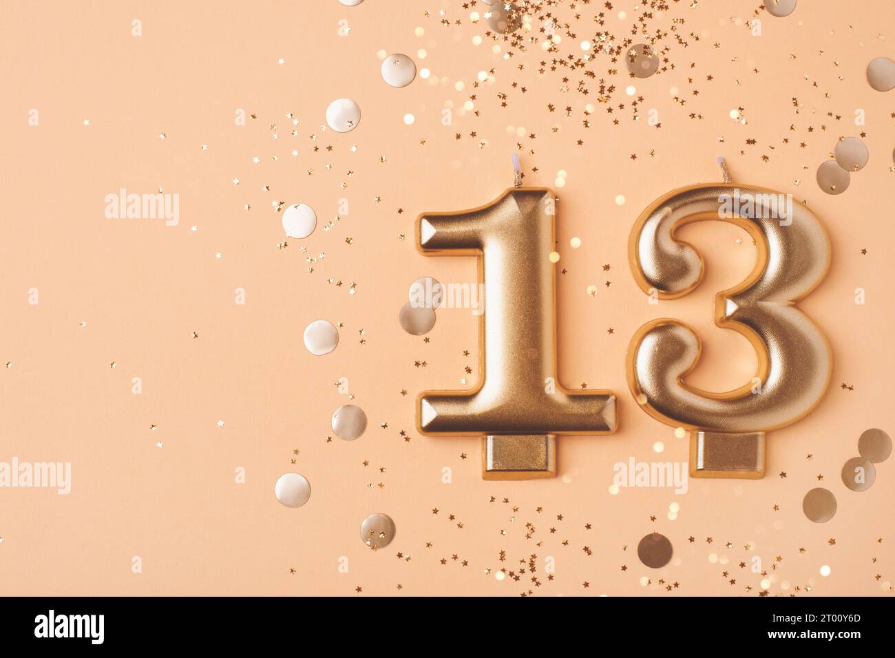 Gold candles in the form of number thirteen on peach background with ...