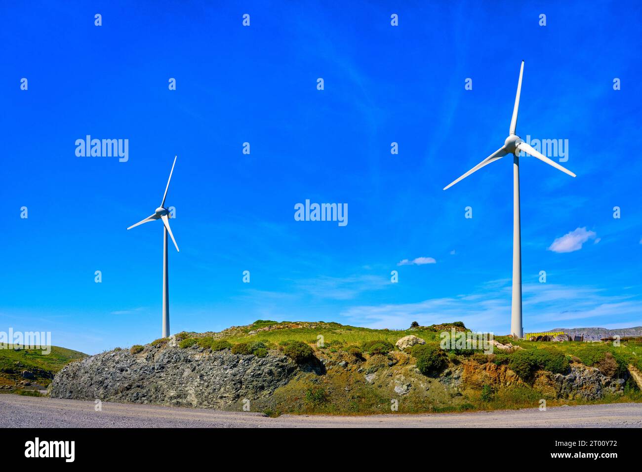Two wind turbines on top of green hill on sunny day. Local energy ...