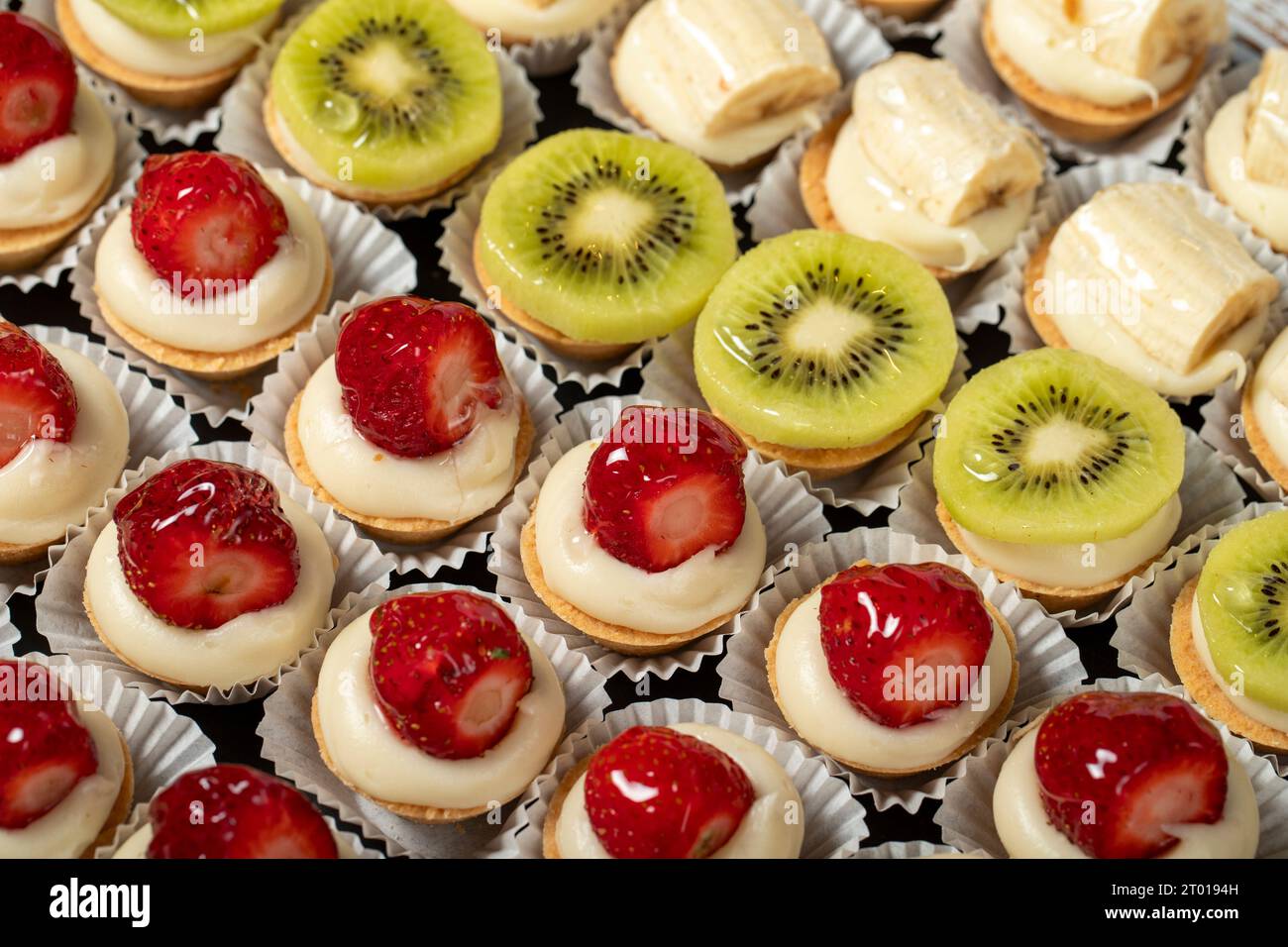 Fruit tartlet. Banana, kiwi and strawberry tartlets on a white ...
