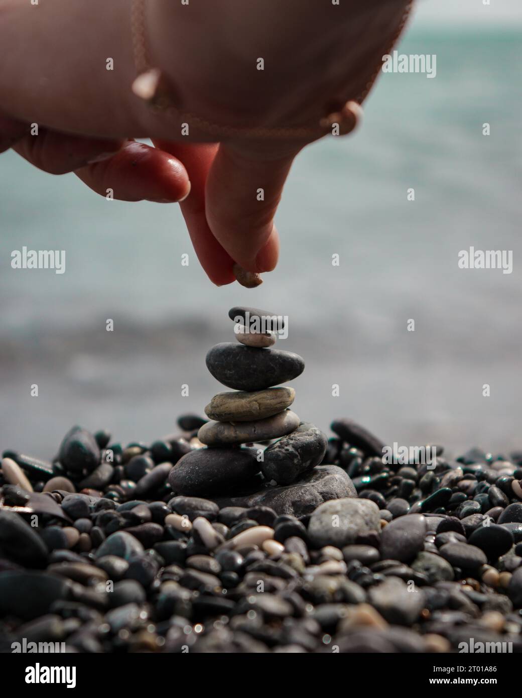 A hand setting pebbles on top of each other to form a pyramid on a ...