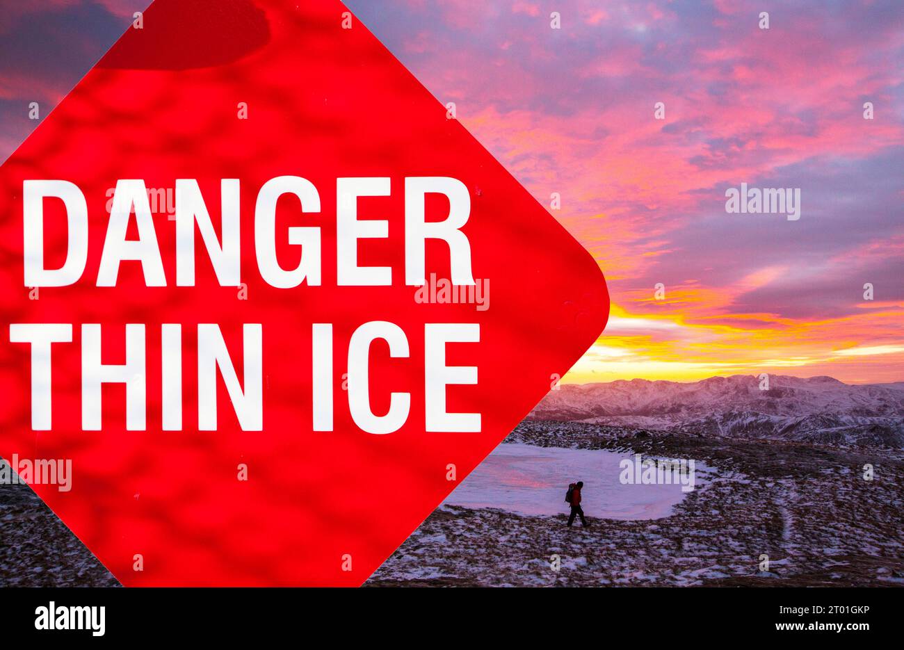 A mountaineer infront of a frozen tarn on the summit of Red Screes ...