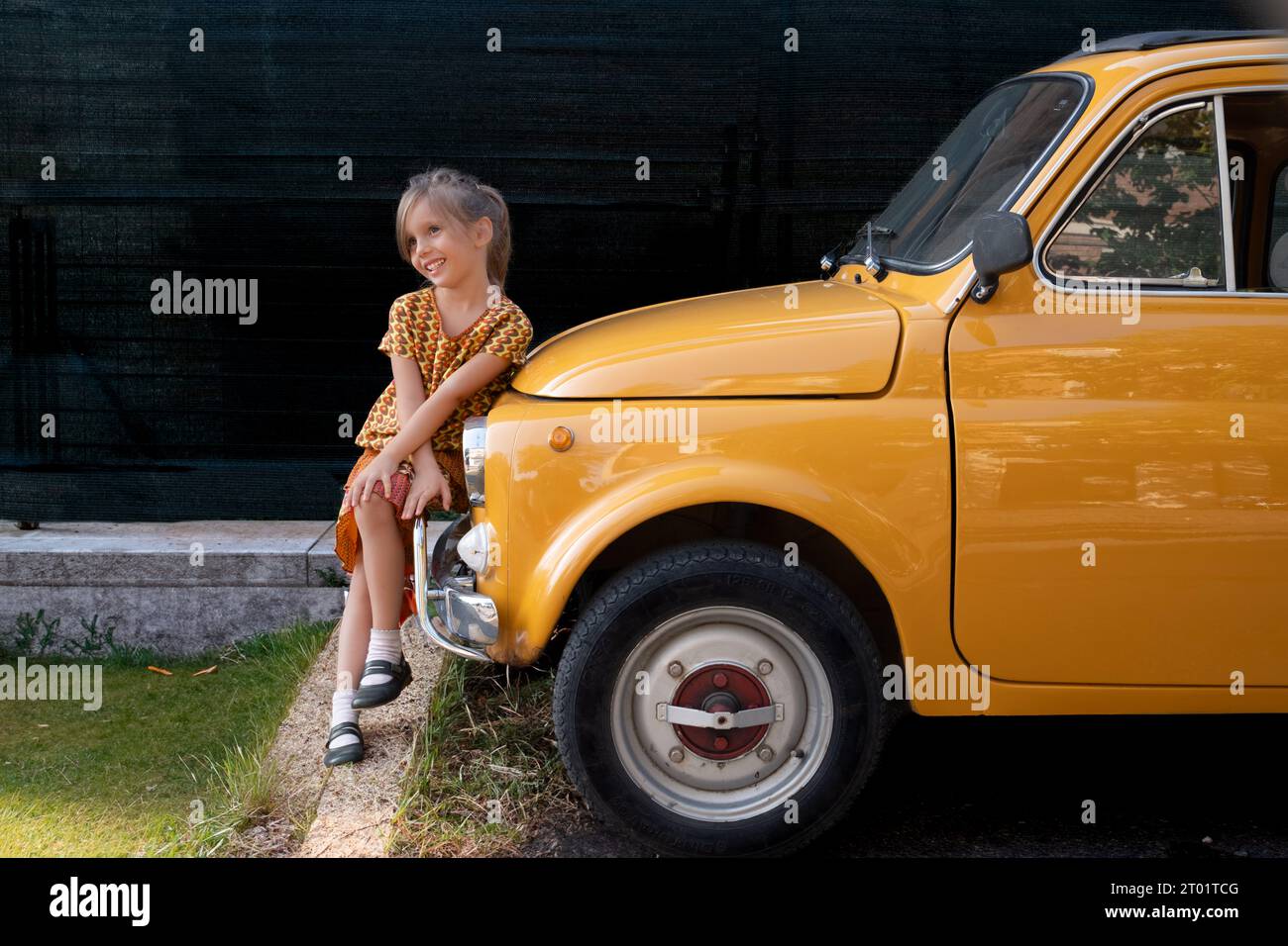 Smiling young girl leaning a fiat 500 classic car dressed in the same ...