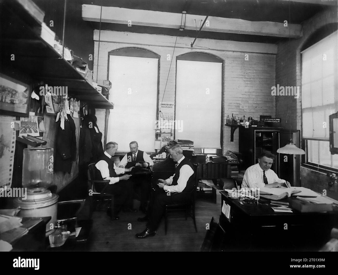A scene within an office, typical of the 1920s. A group of four men ...