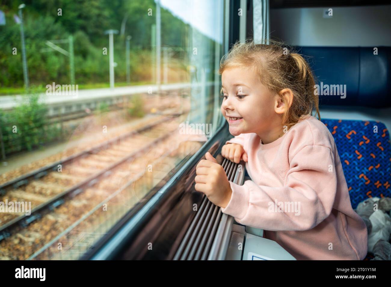 Happy little girl looking out train window outside, while it moving ...