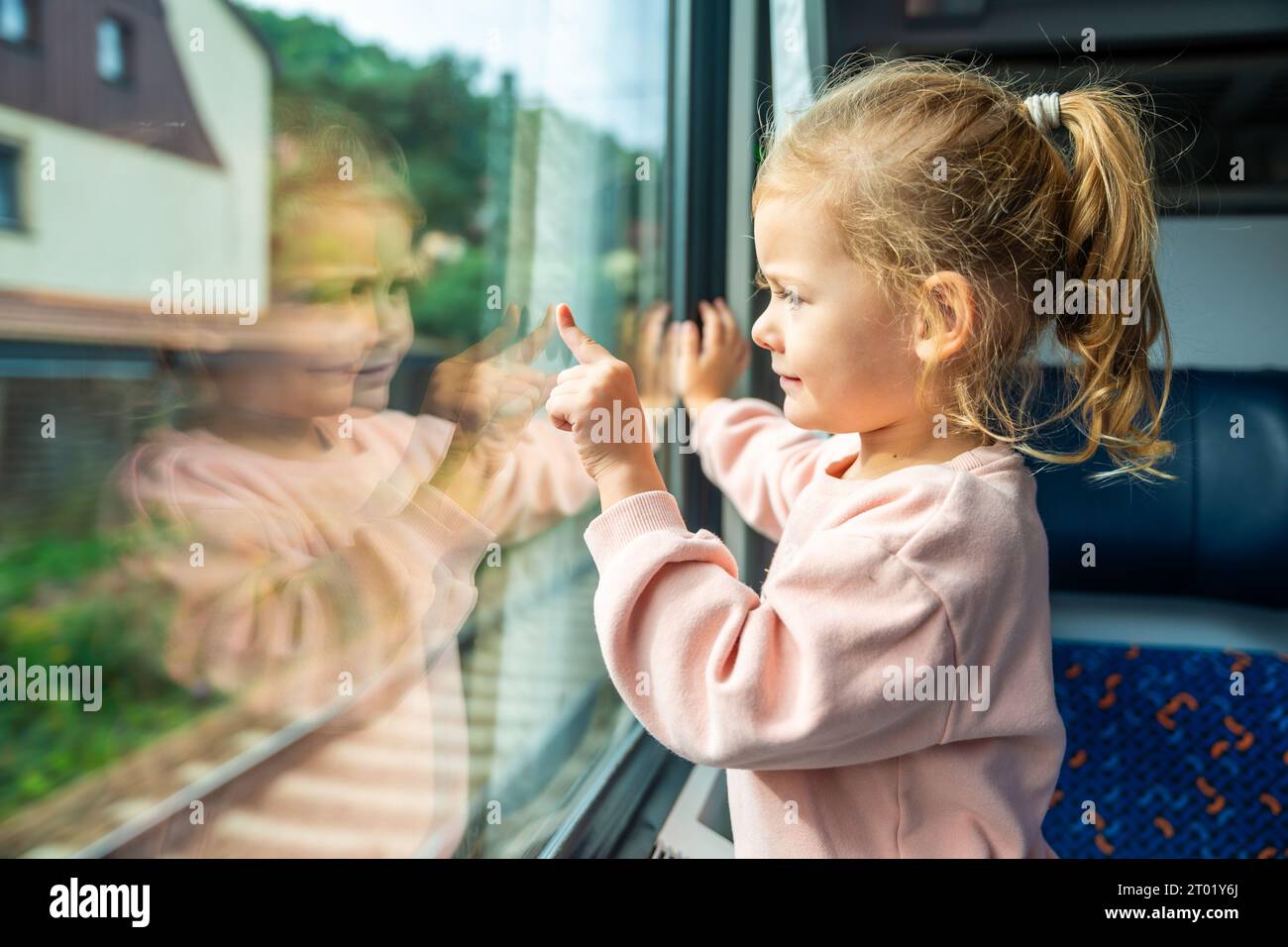 Beautiful little girl looking out train window outside, while it moving ...