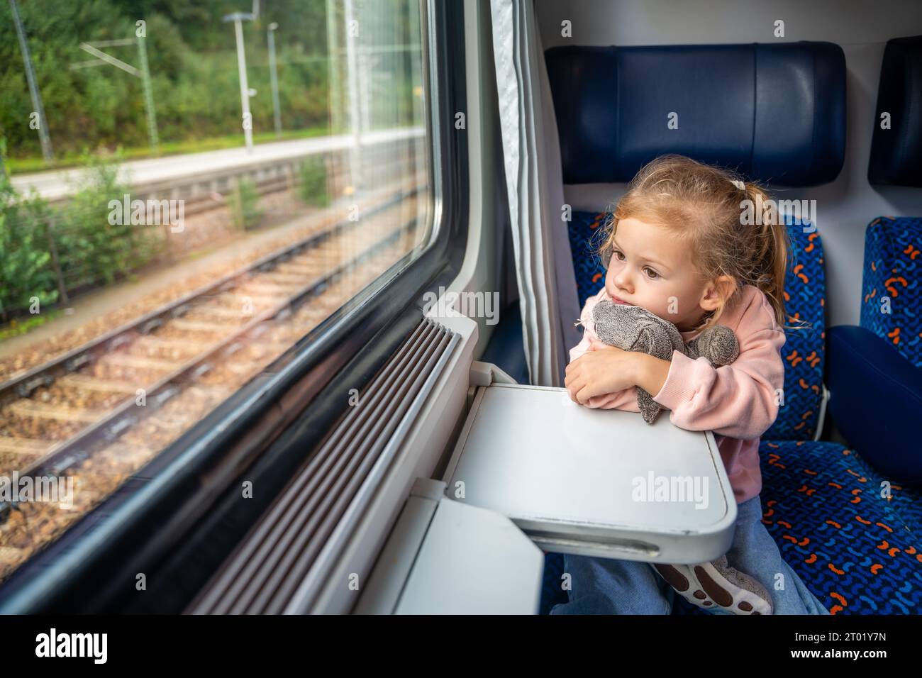 Bored little girl with toy looking out train window outside, while it ...