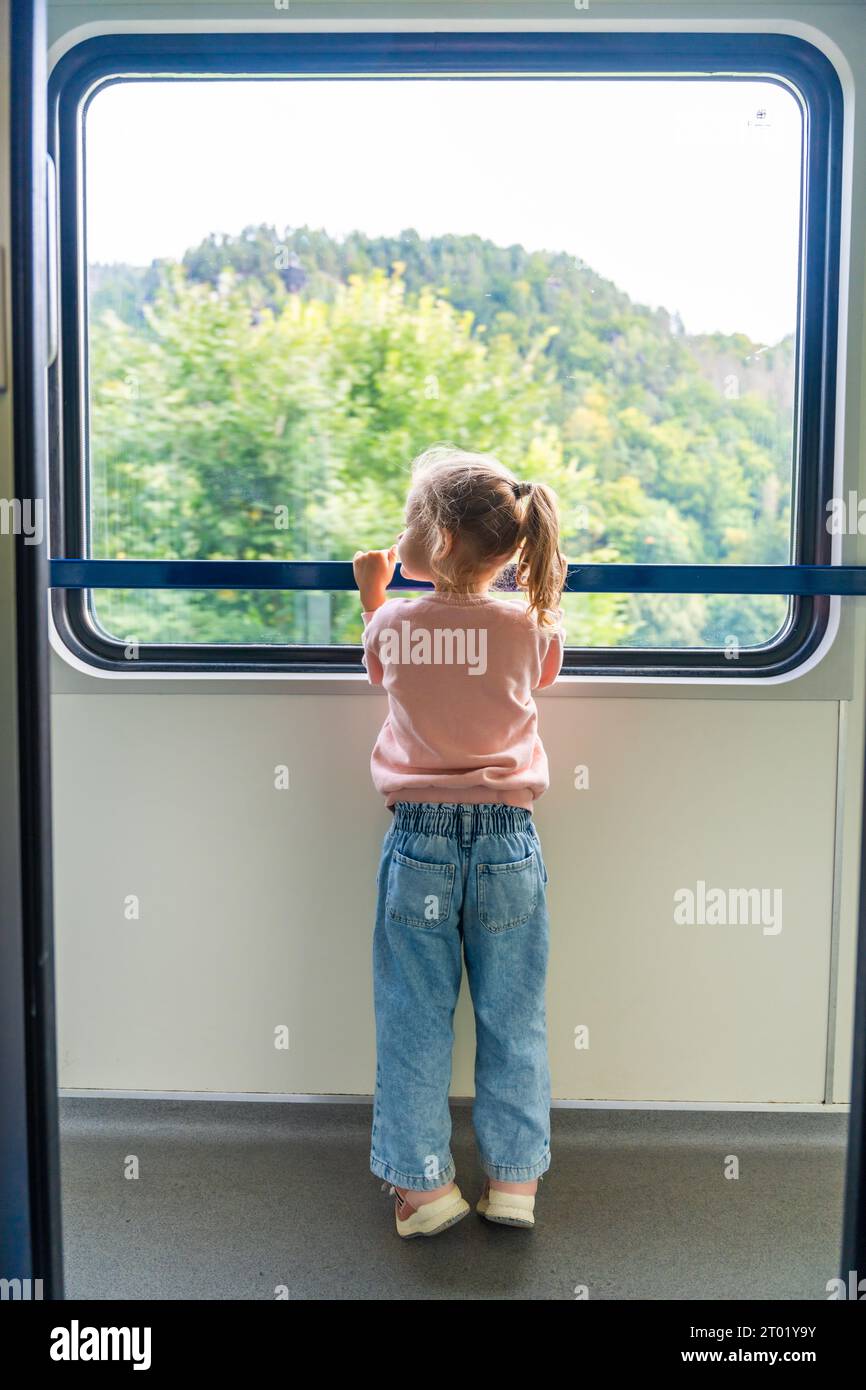 Little girl looking out train window outside, while it moving ...