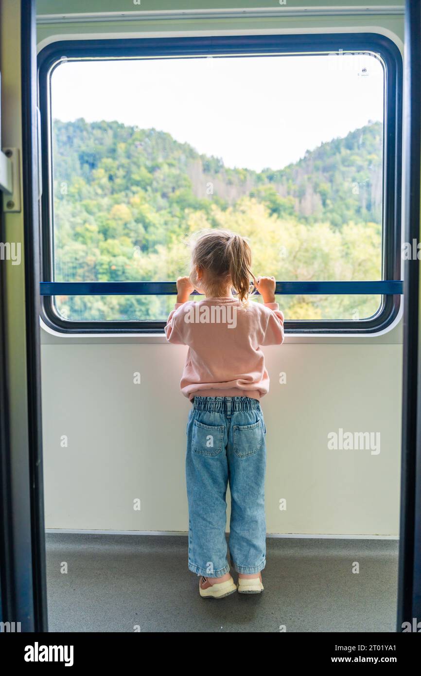 Beautiful little girl looking out train window outside, while it moving ...
