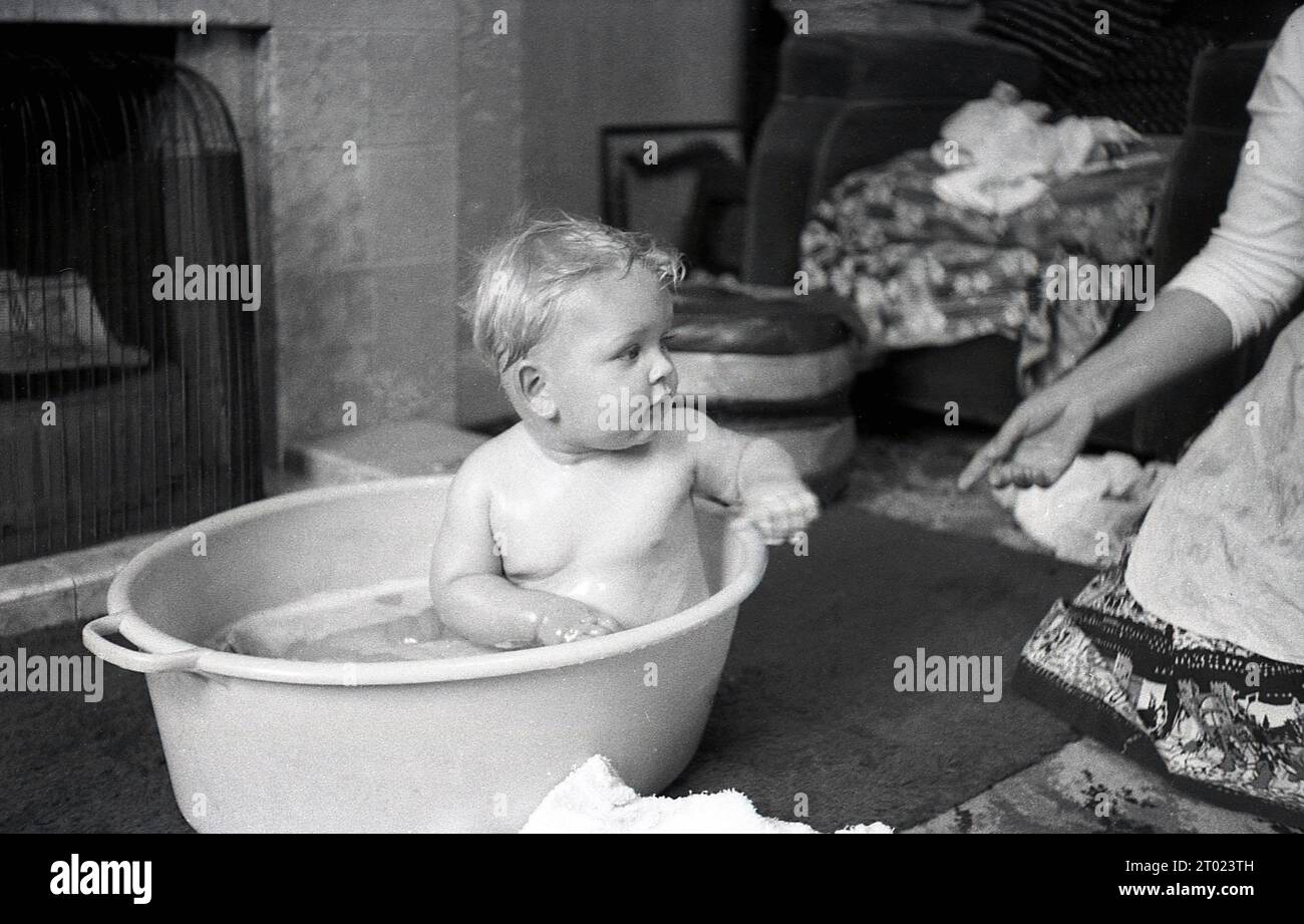 1960s, historical, bathtime, a infant boy sitting in a plastic bow sat ...