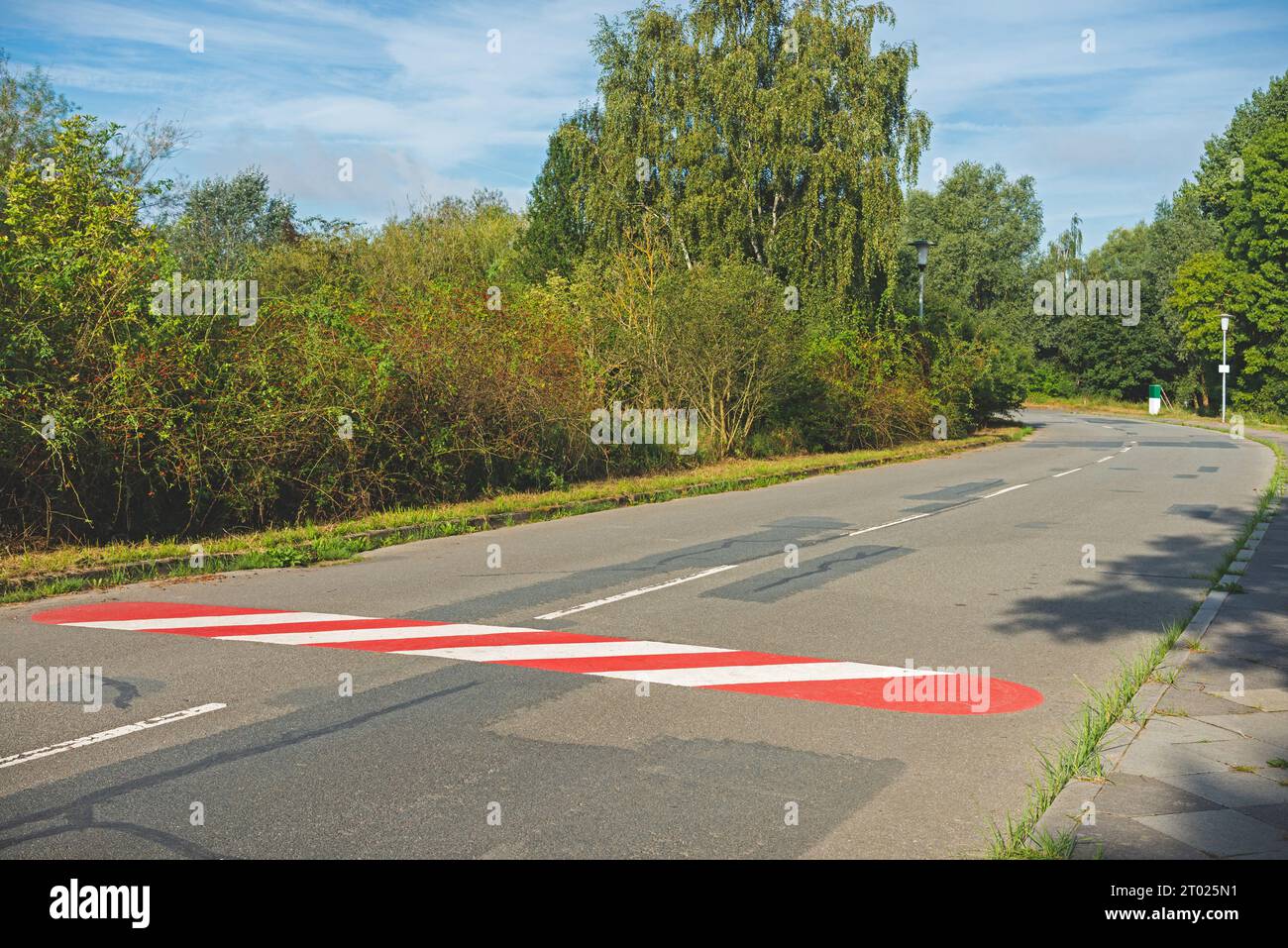 Red and white speed bump on asphalt road for slowing traffic next to ...