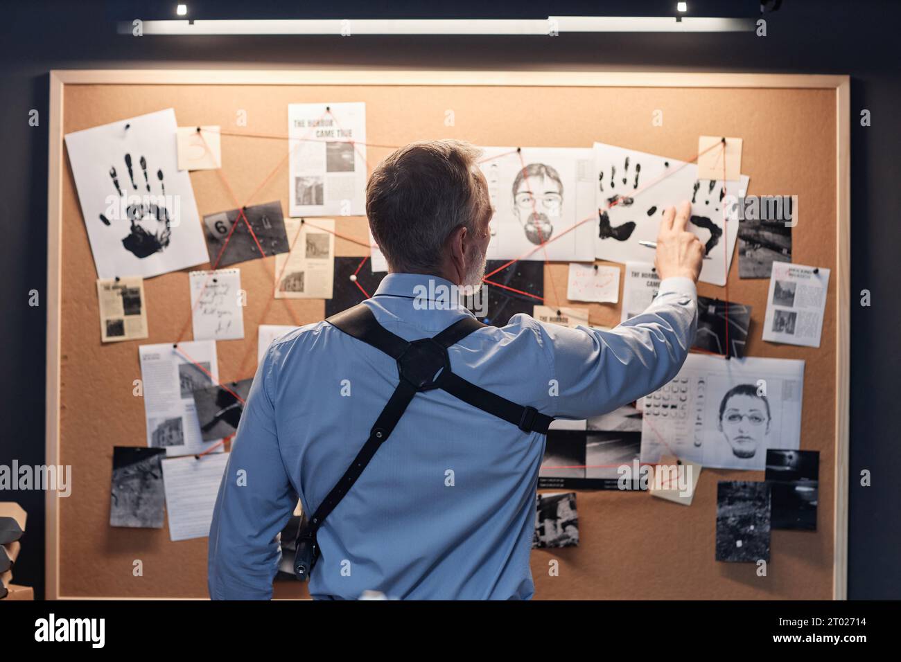 Back view of senior detective standing by evidence board and studying ...