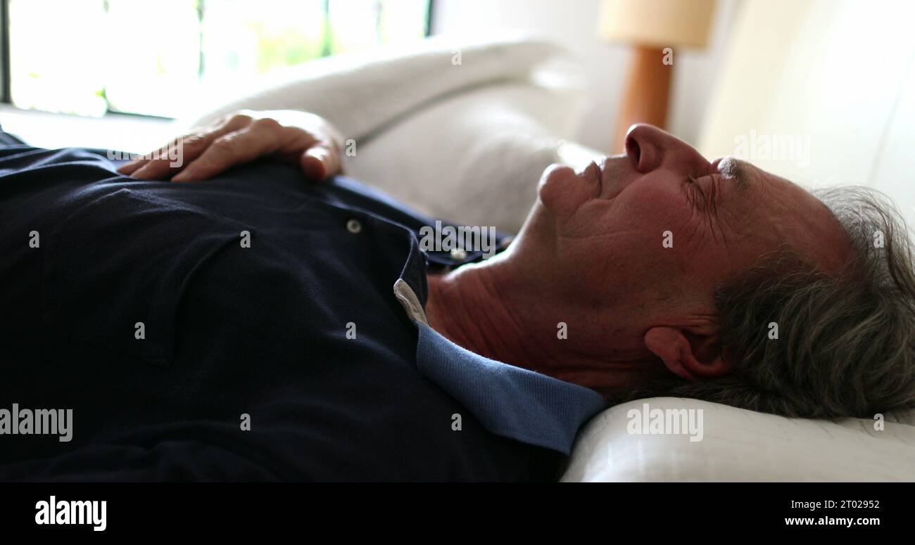 Older man lies in bed to rest, senior looks at camera while laying down ...