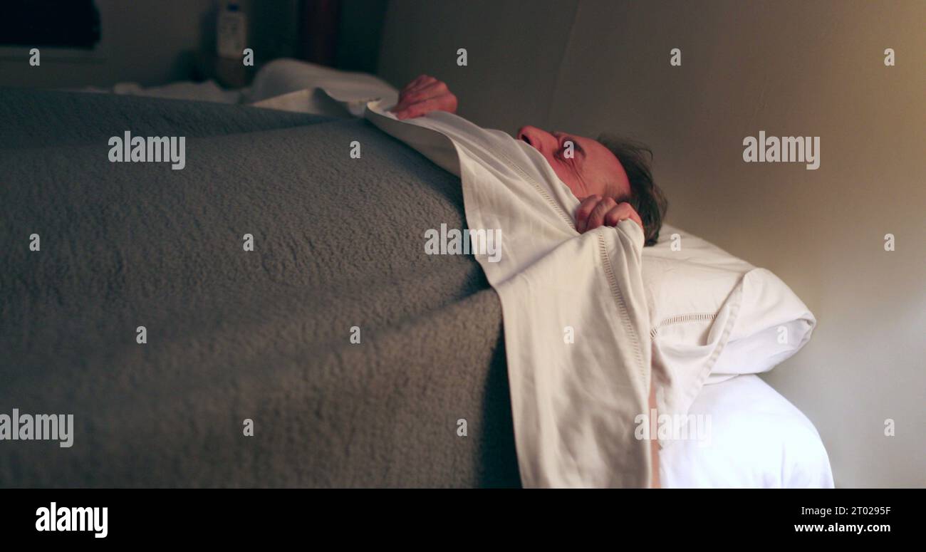 Older man lying down in bed at night turning off nightstand lamp light ...