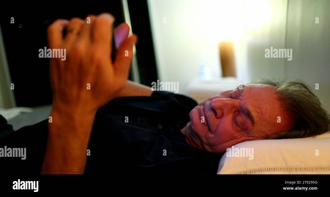Older man looking at cellphone screen at night laying down in bed Stock ...