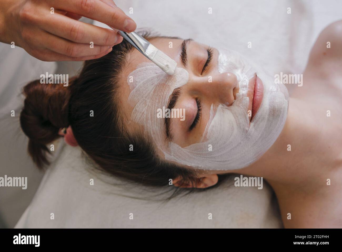 Beautician's hands covering woman facial skin with moisturizing mask ...