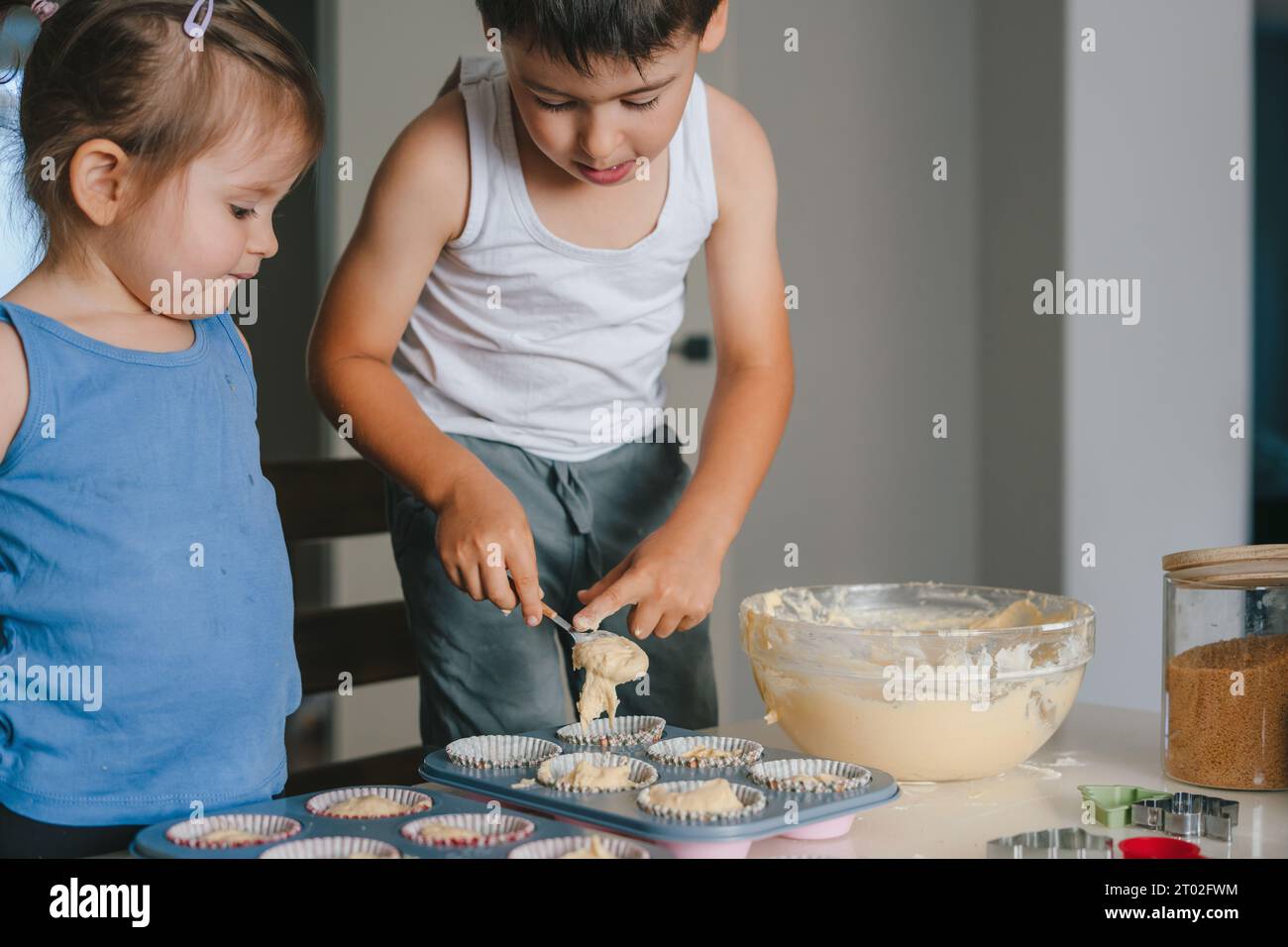 Cute little girl and her brother are spooning muffin batter into the ...