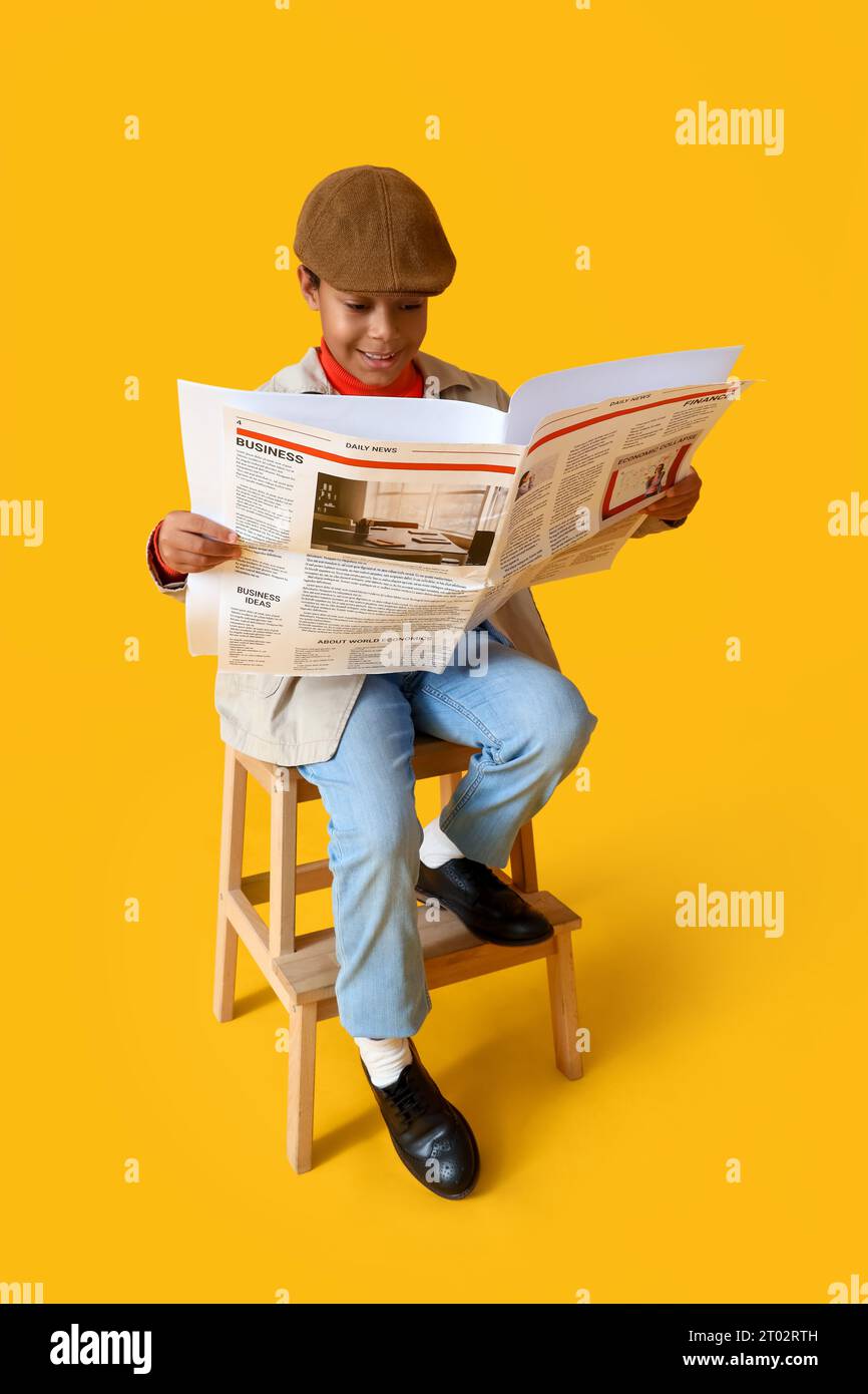 African-American little boy reading newspaper on yellow background ...