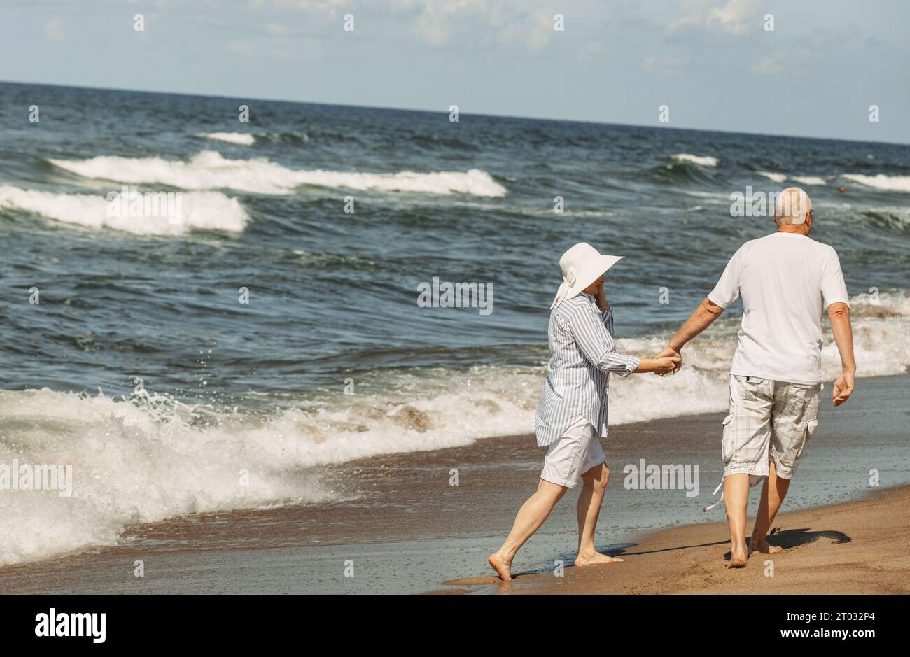 An elderly couple walk along the seashore, relax, communicate. Waves ...
