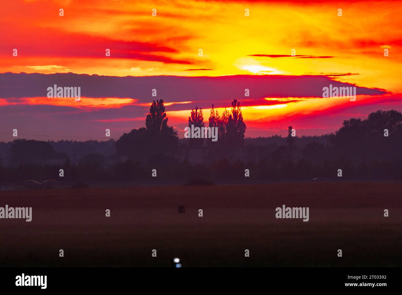 Beautiful cloudy red sunset with gigantic sun over big fields and trees ...