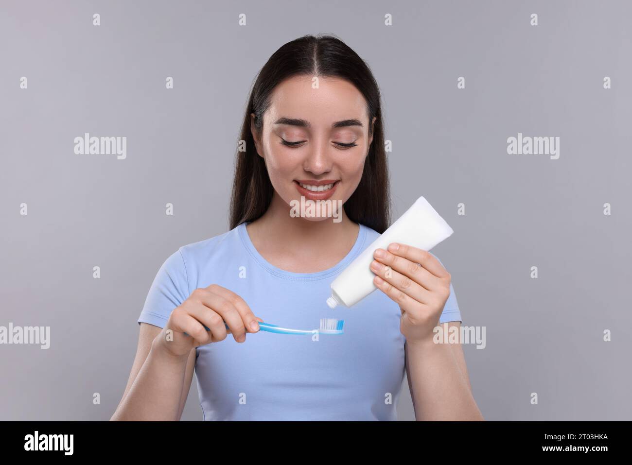 Happy woman squeezing toothpaste from tube onto plastic toothbrush on ...