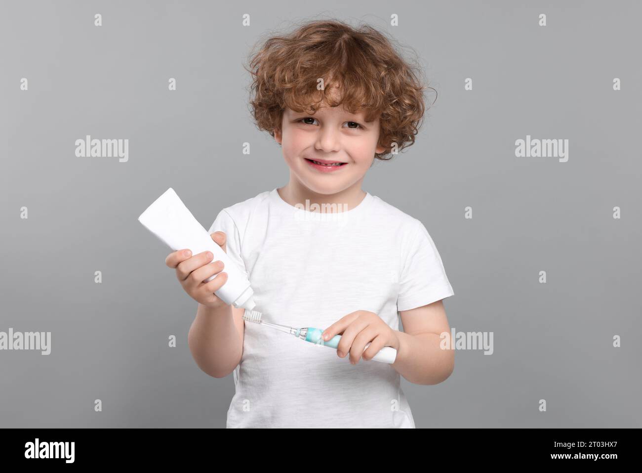 Cute little boy squeezing toothpaste from tube onto electric toothbrush ...