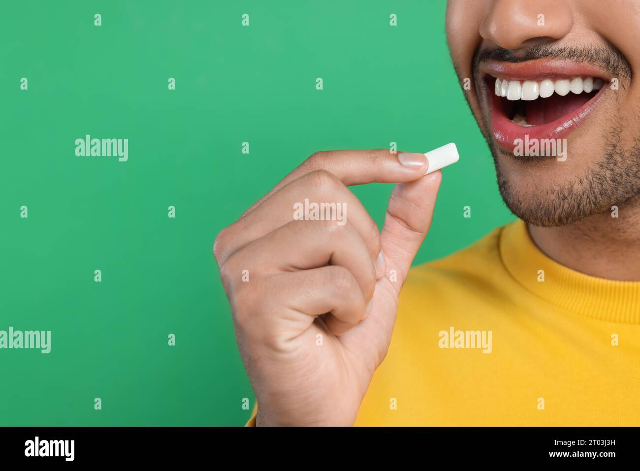 Happy man putting bubble gum into mouth on green background, closeup ...