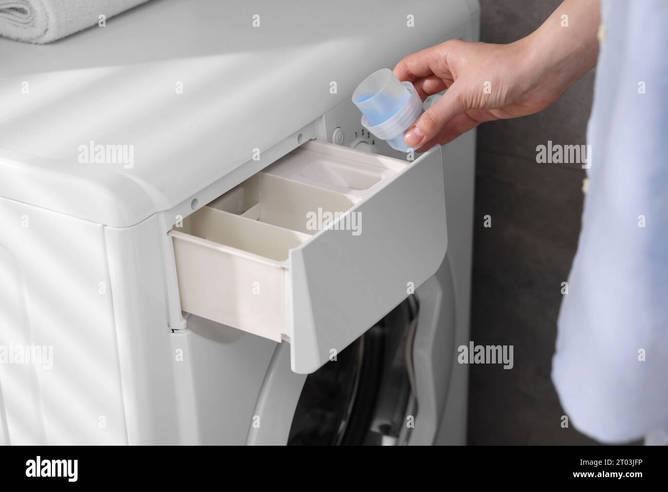 Woman pouring fabric softener from cap into washing machine near grey ...