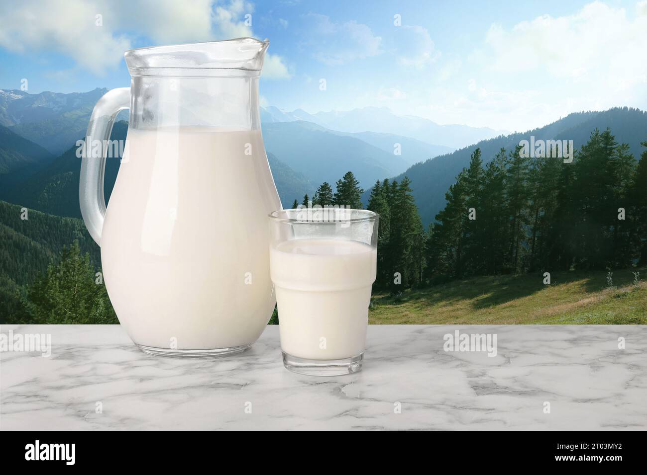 Fresh milk in glass and pitcher on white marble table against mountain ...