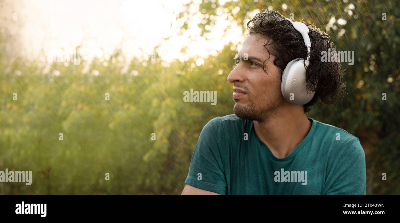 Portrait of an upset guy freezing in the rain while walking in the park ...