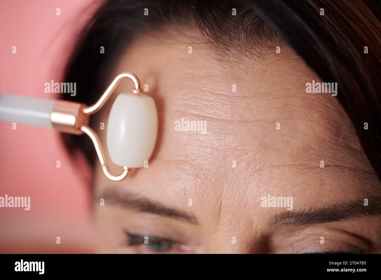 Closeup image of woman massaging forehead with roller to reduce ...