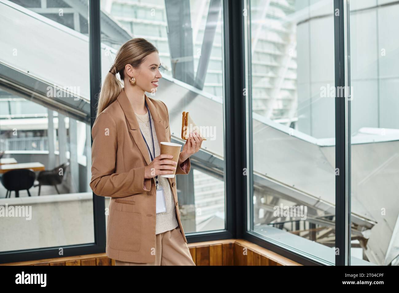 happy blonde woman enjoying her sandwich and coffee during lunch break at work, coworking ...