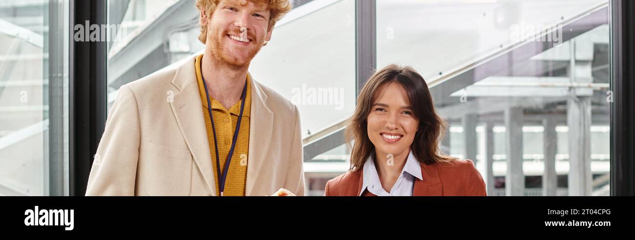 two cheerful team members smiling and looking at camera with glass on ...