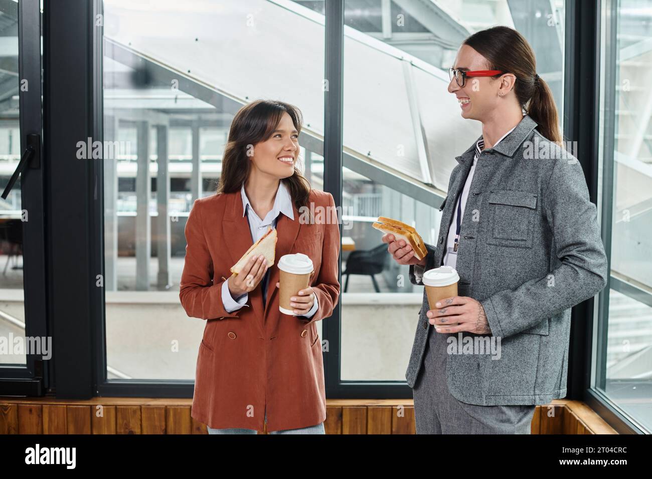two young colleagues having sandwich with tea on break and smiling at ...
