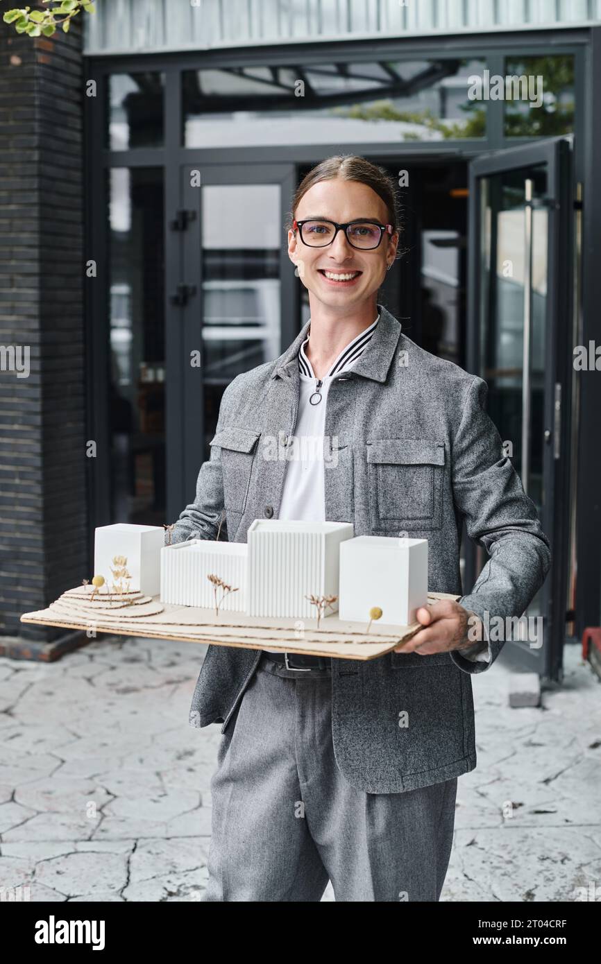 young cheerful man in glasses with scale model of building looking at ...