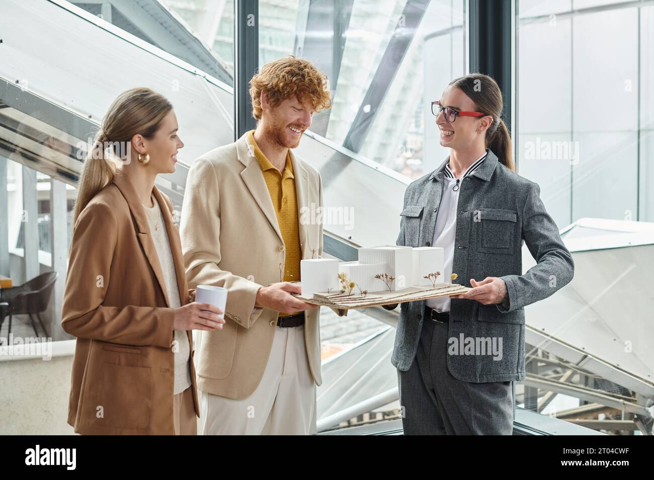 three cheerful coworkers holding scale model and tea cup while doing ...