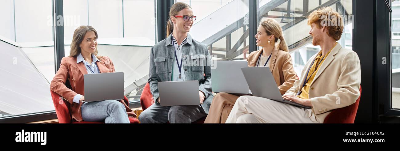 four smiley colleagues smiling and working on laptops with glass ...