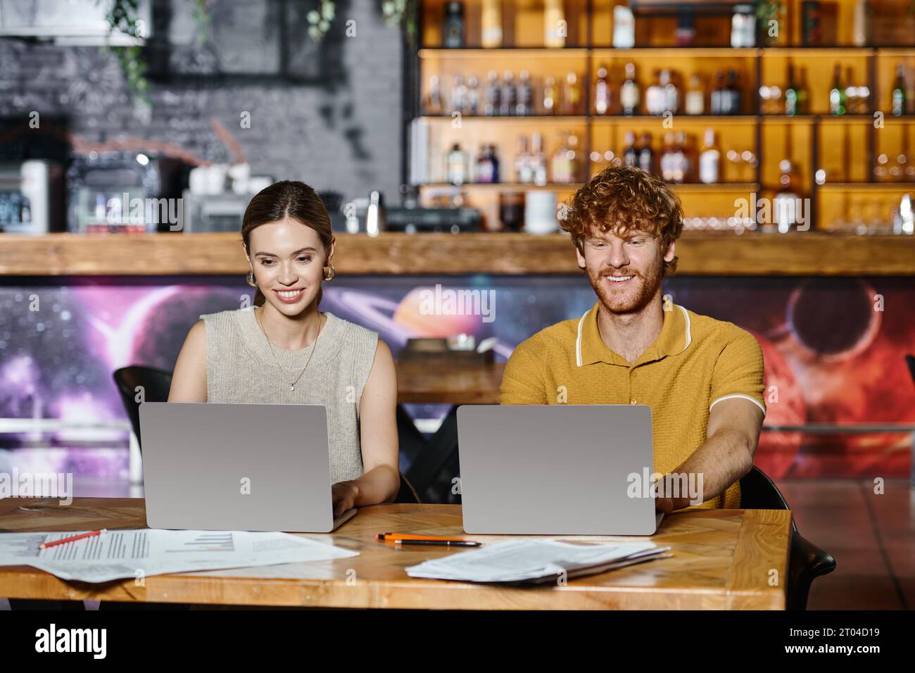 two cheerful colleagues smiling while working on laptops with blurred ...