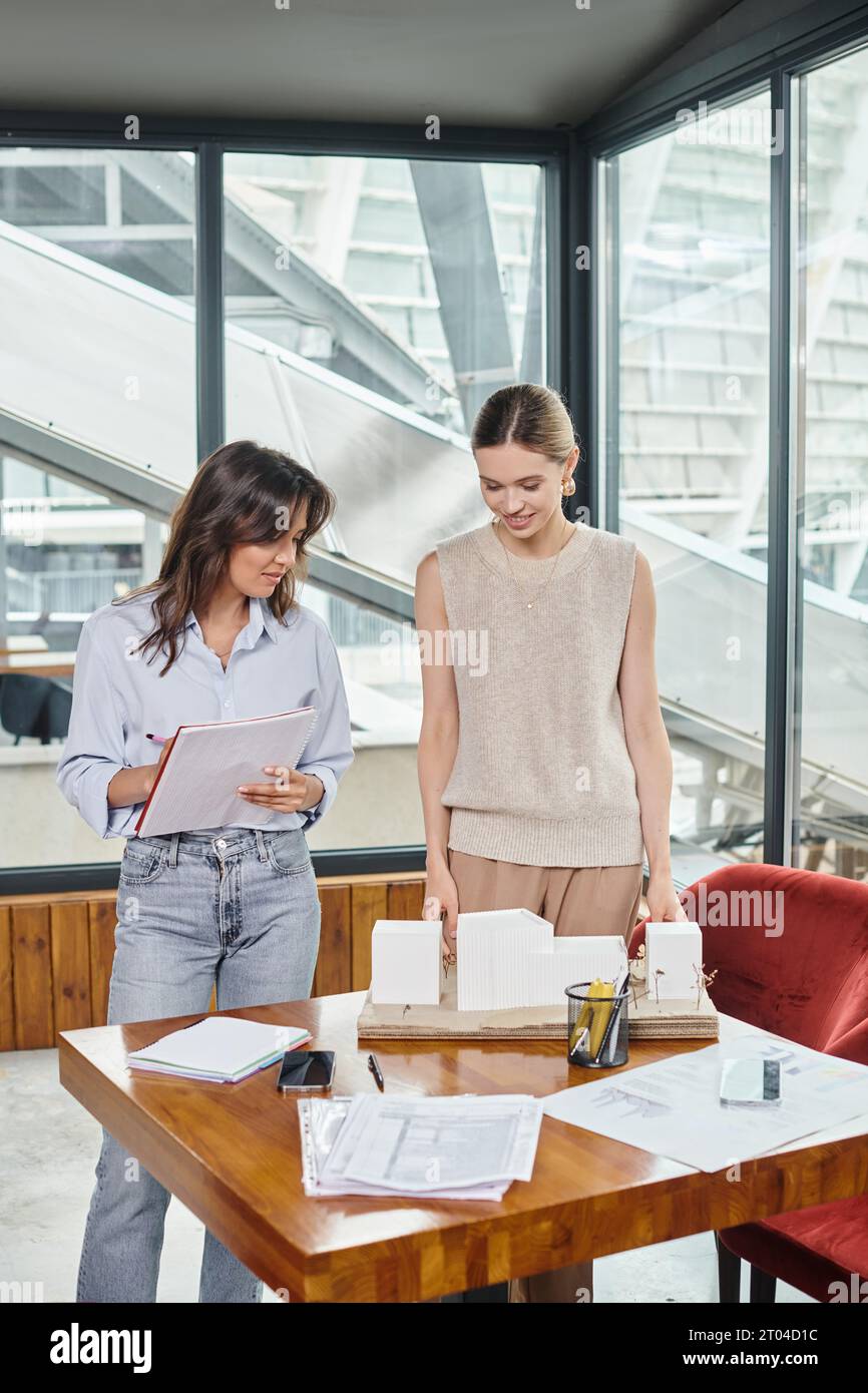 two team members focused on scale model and paperwork with glass on ...