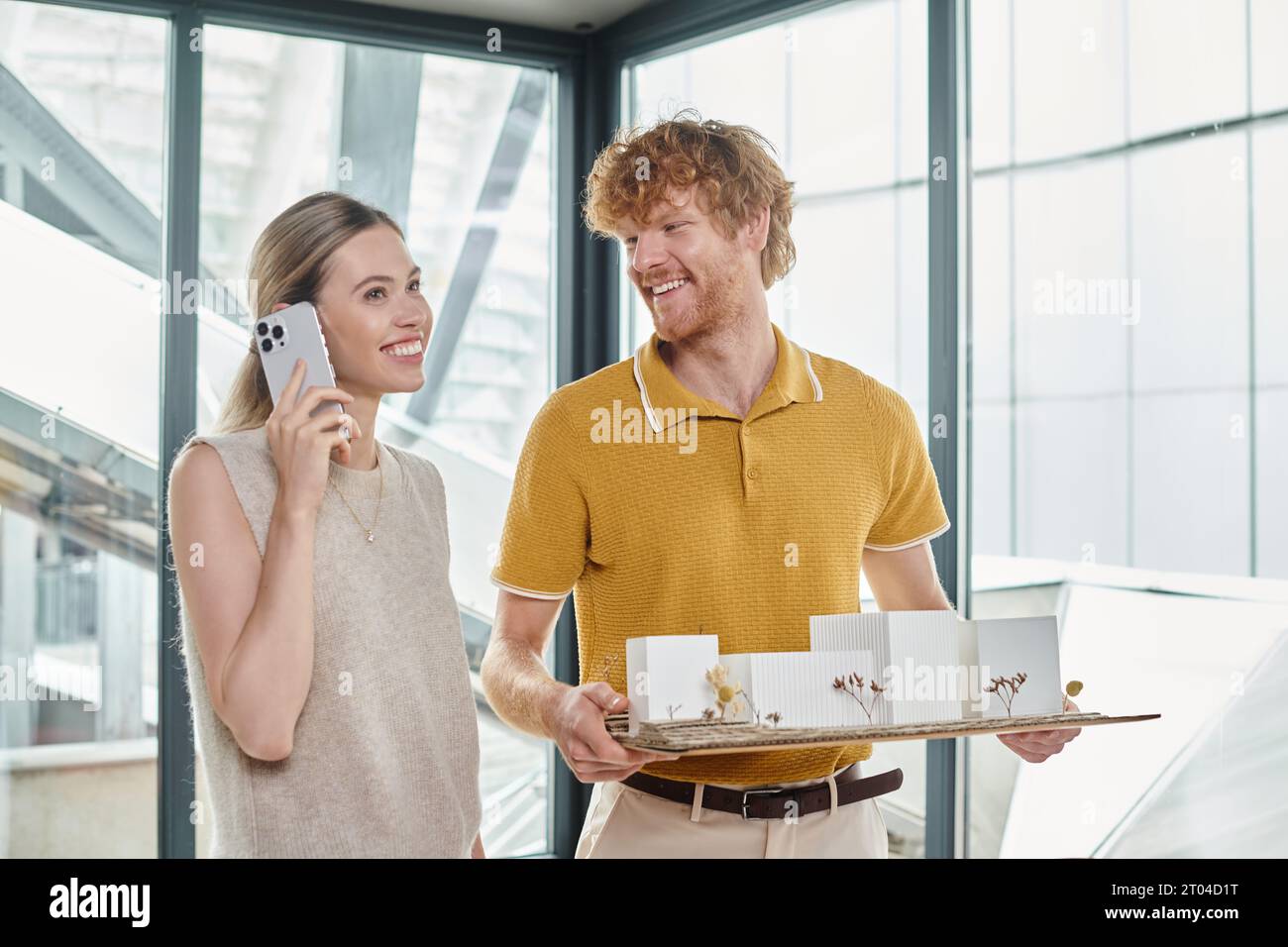 cheerful team members working with building model and talking on mobile ...