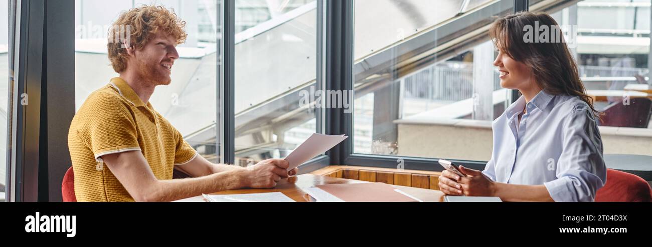two cheerful colleagues in smart attire with papers looking at each ...