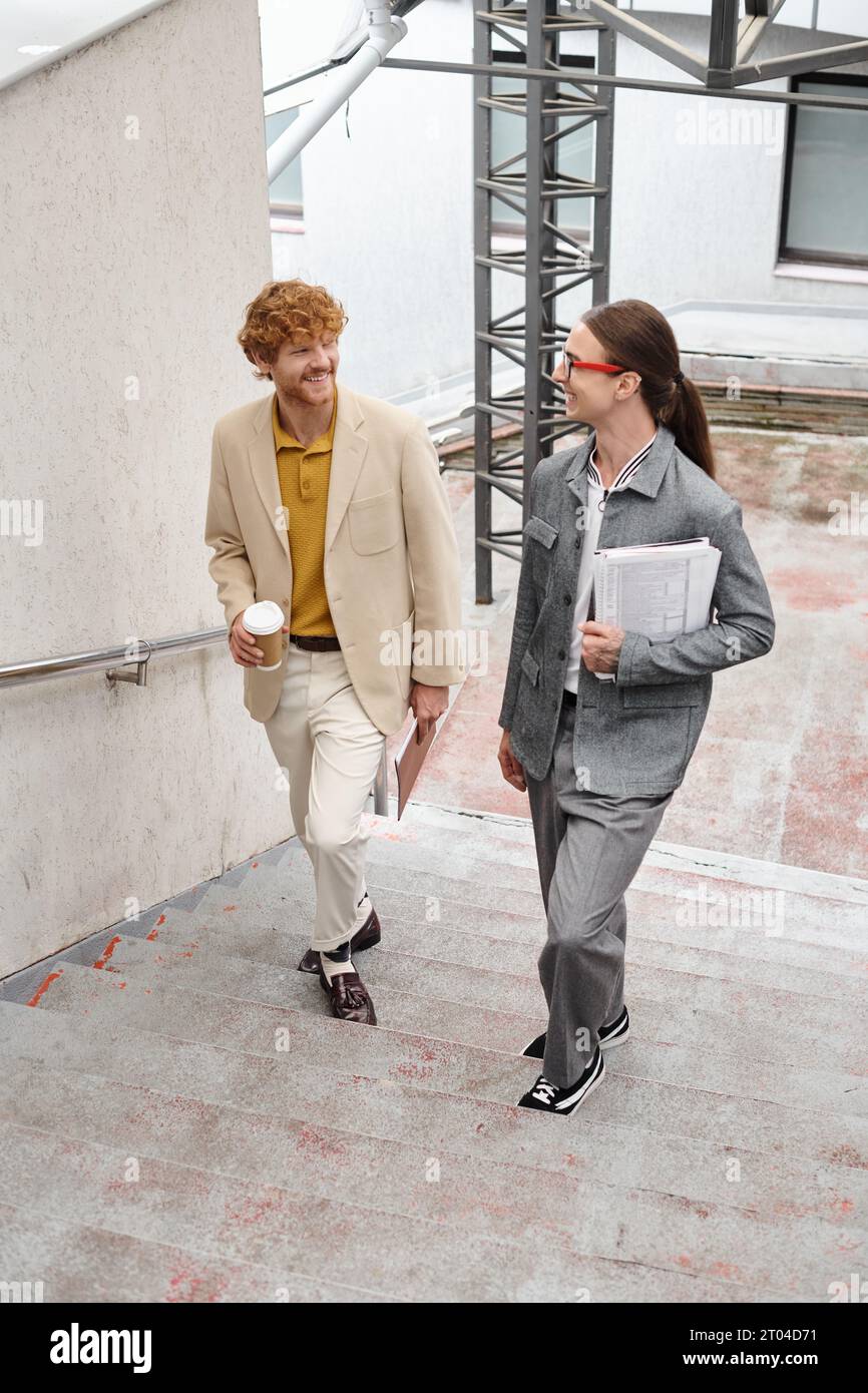 two young male colleagues walking upstairs talking and smiling at each ...
