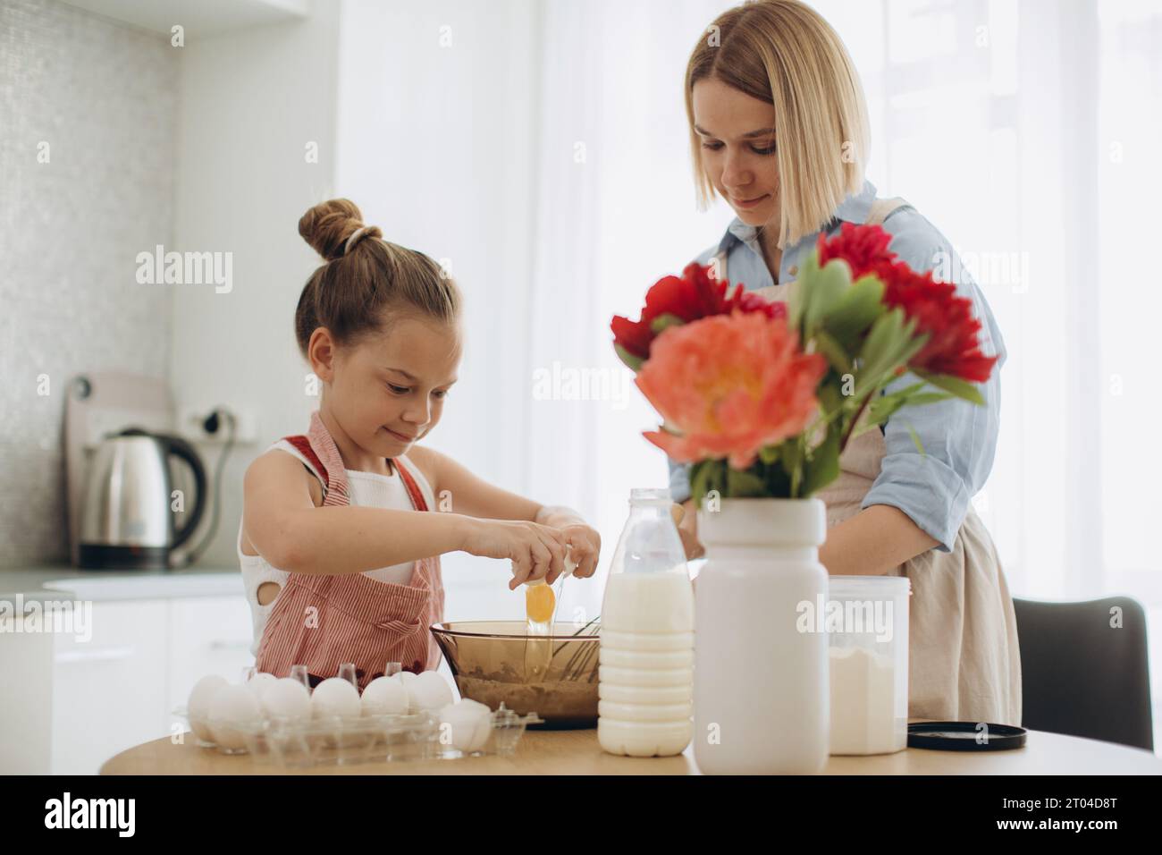 Mother and daughter prepare pancake batter. A mother teaches her 8-year ...
