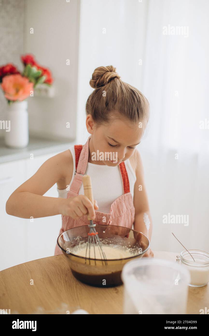 A cute little girl in an apron is preparing pancake batter in the ...