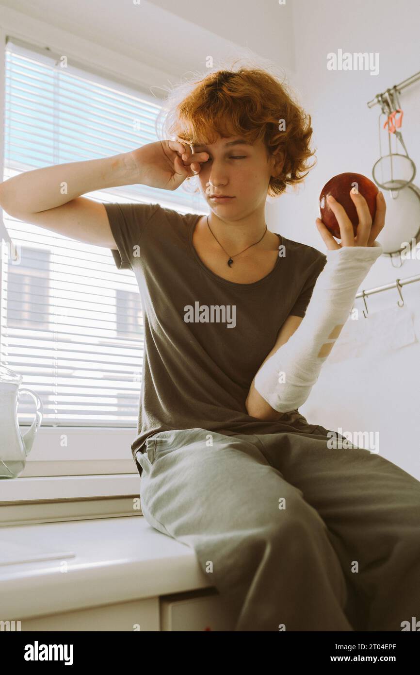 teenage girl with broken arm in cast in kitchen sitting on countertop ...