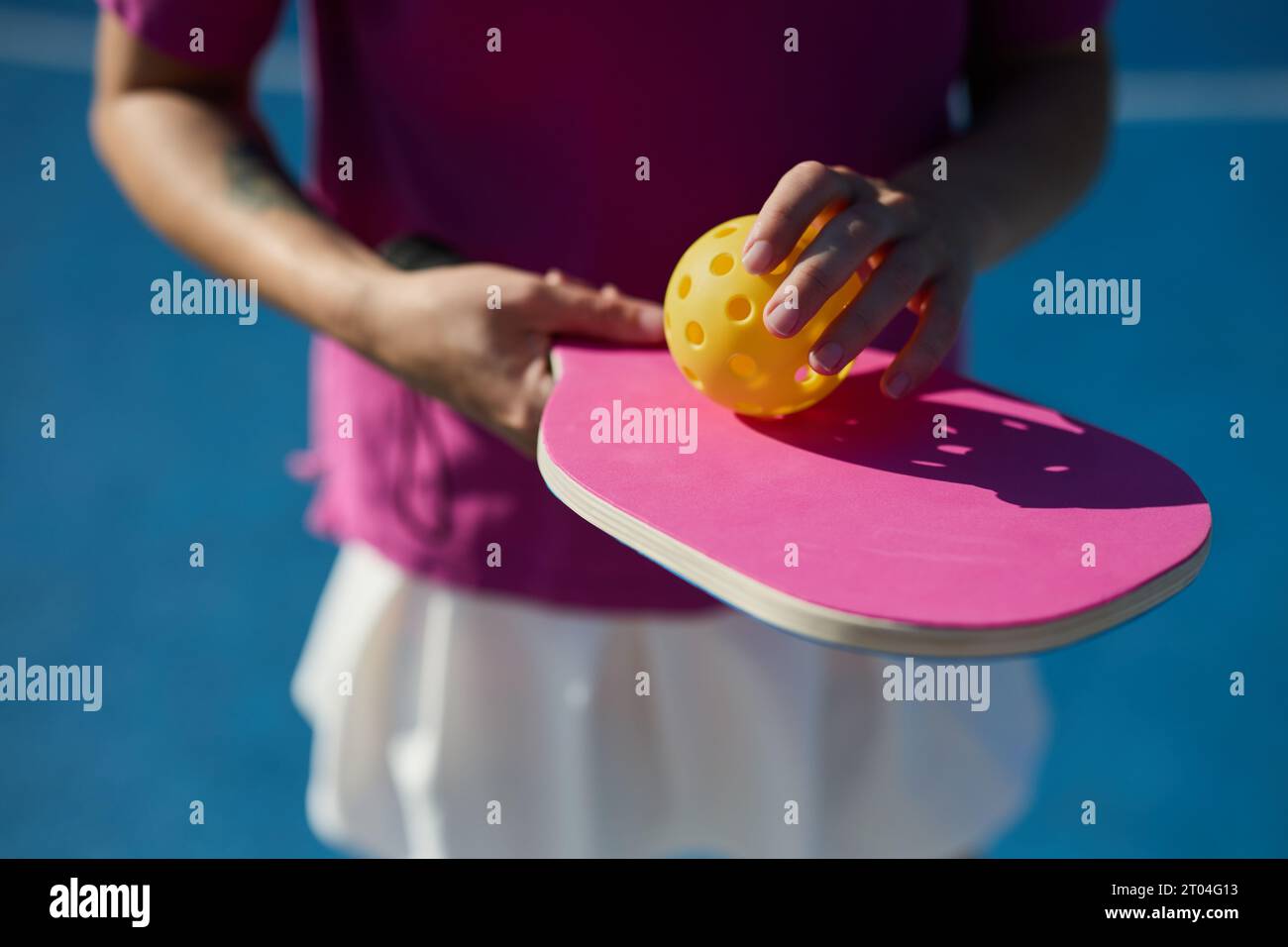 Female pickler holding a pickleball racket and perforated plastic ball ...