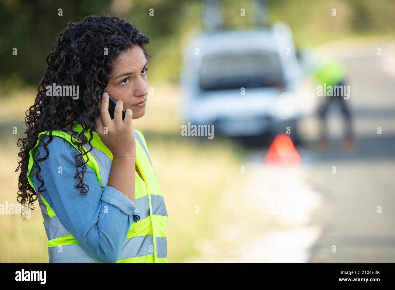 young female driver wearing a high visibility vest calling assistance ...