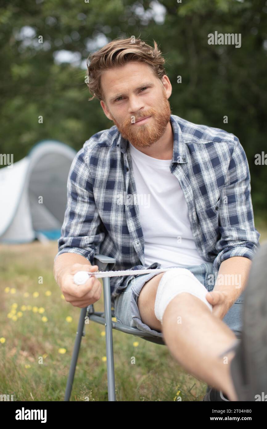 man bandaging his knee while on camping holiday Stock Photo - Alamy