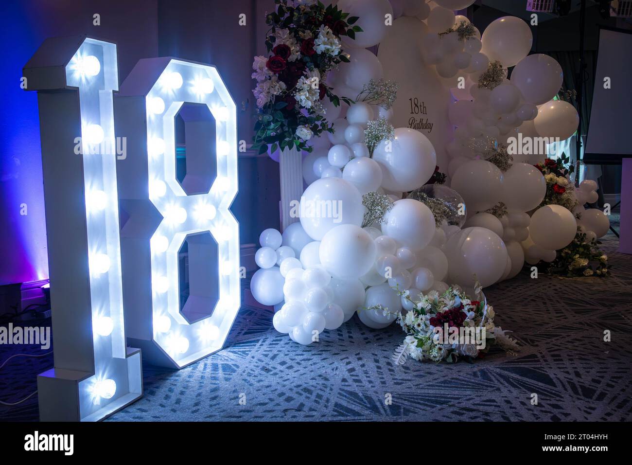 An 18 decorative sign lit up, balloons and a sign form a backdrop at an ...