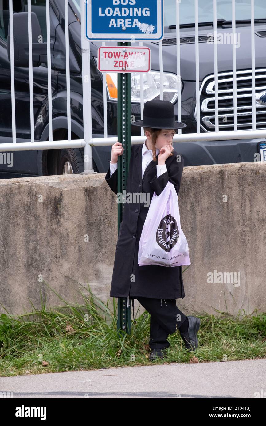 An orthodox Jewish boy with long peyus waits for a bus on Forest Road ...